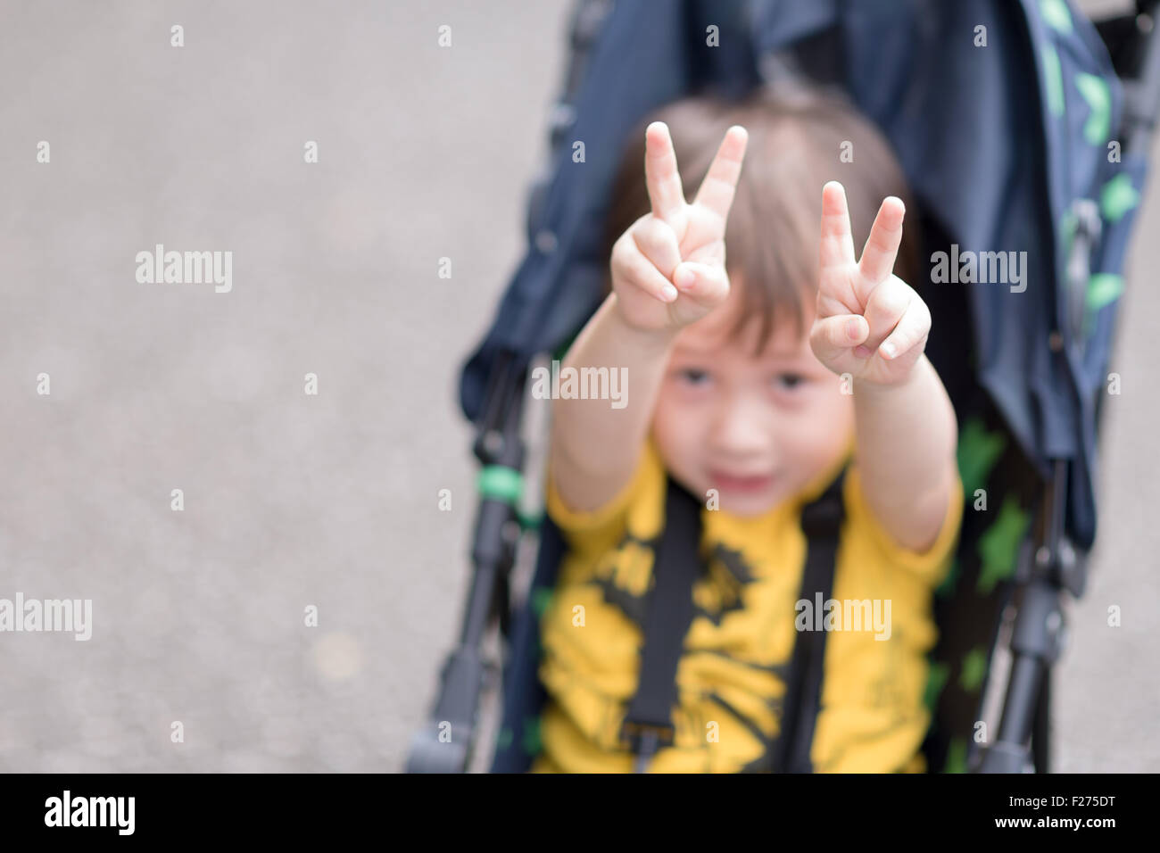 A young boy sitting in a stroller making peace signs with both hands ...
