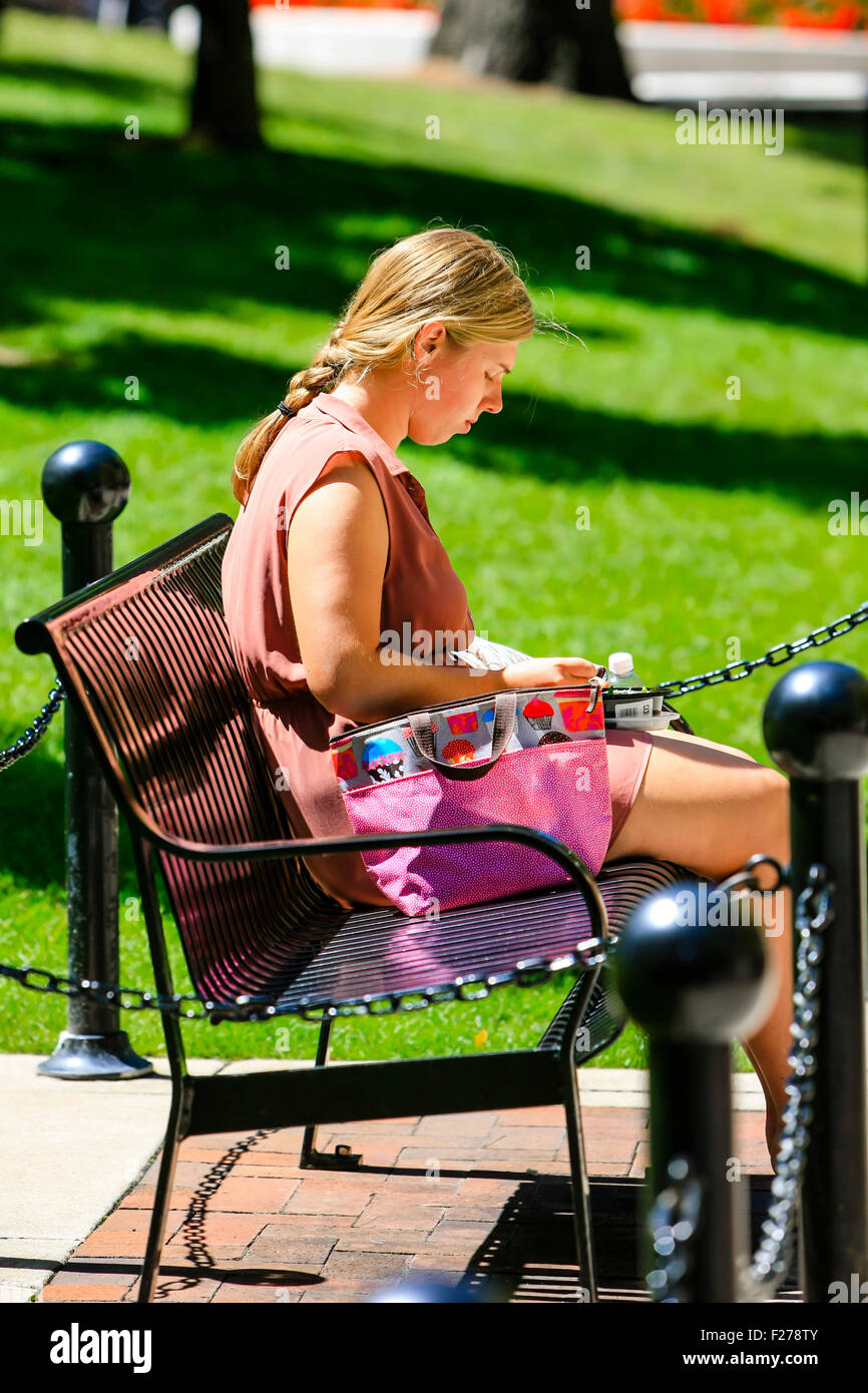Young woman sits on street bench seat eating a snack at lunchtime in ...