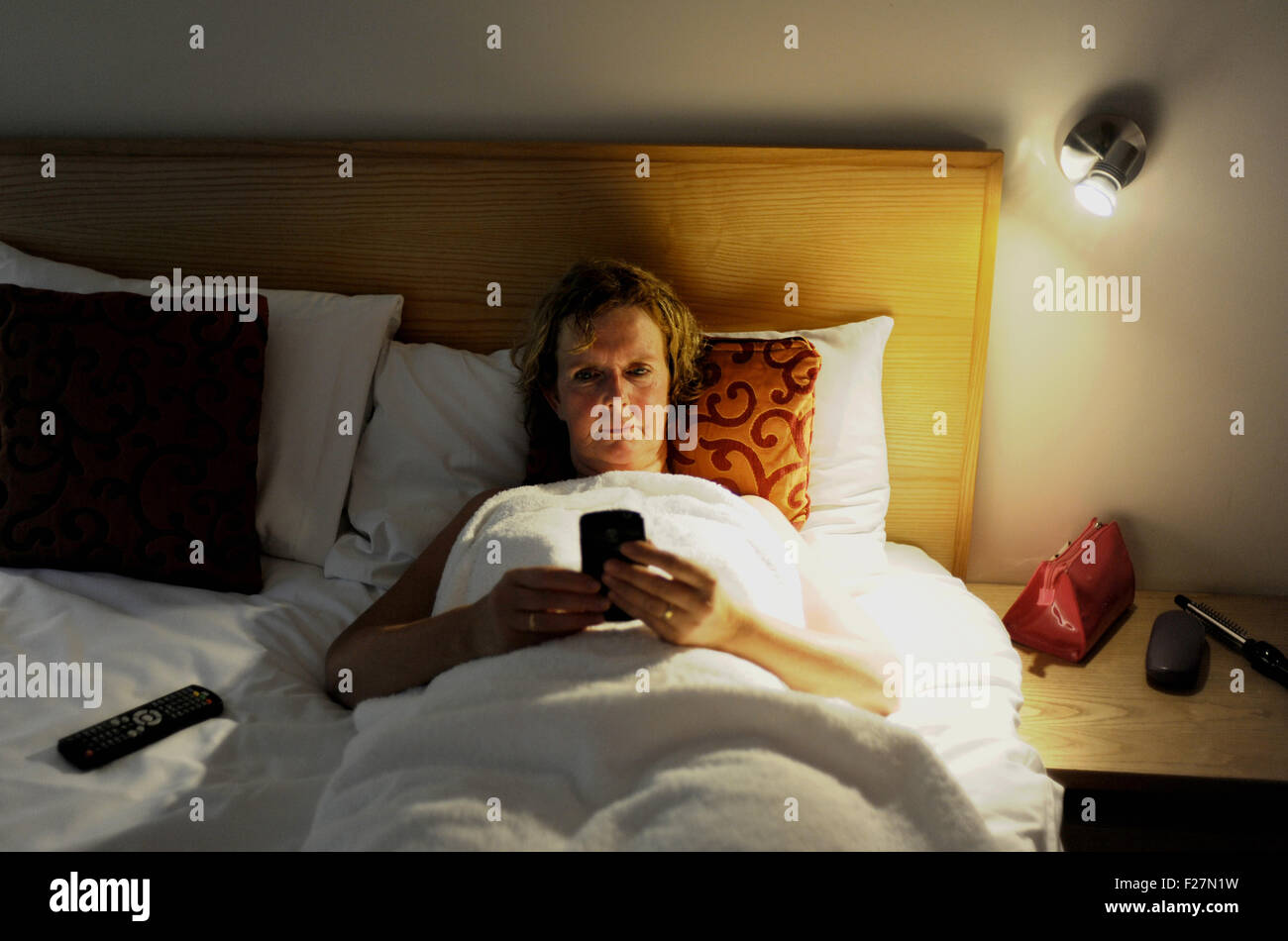 Woman using mobile smart phone in bed by light Stock Photo - Alamy