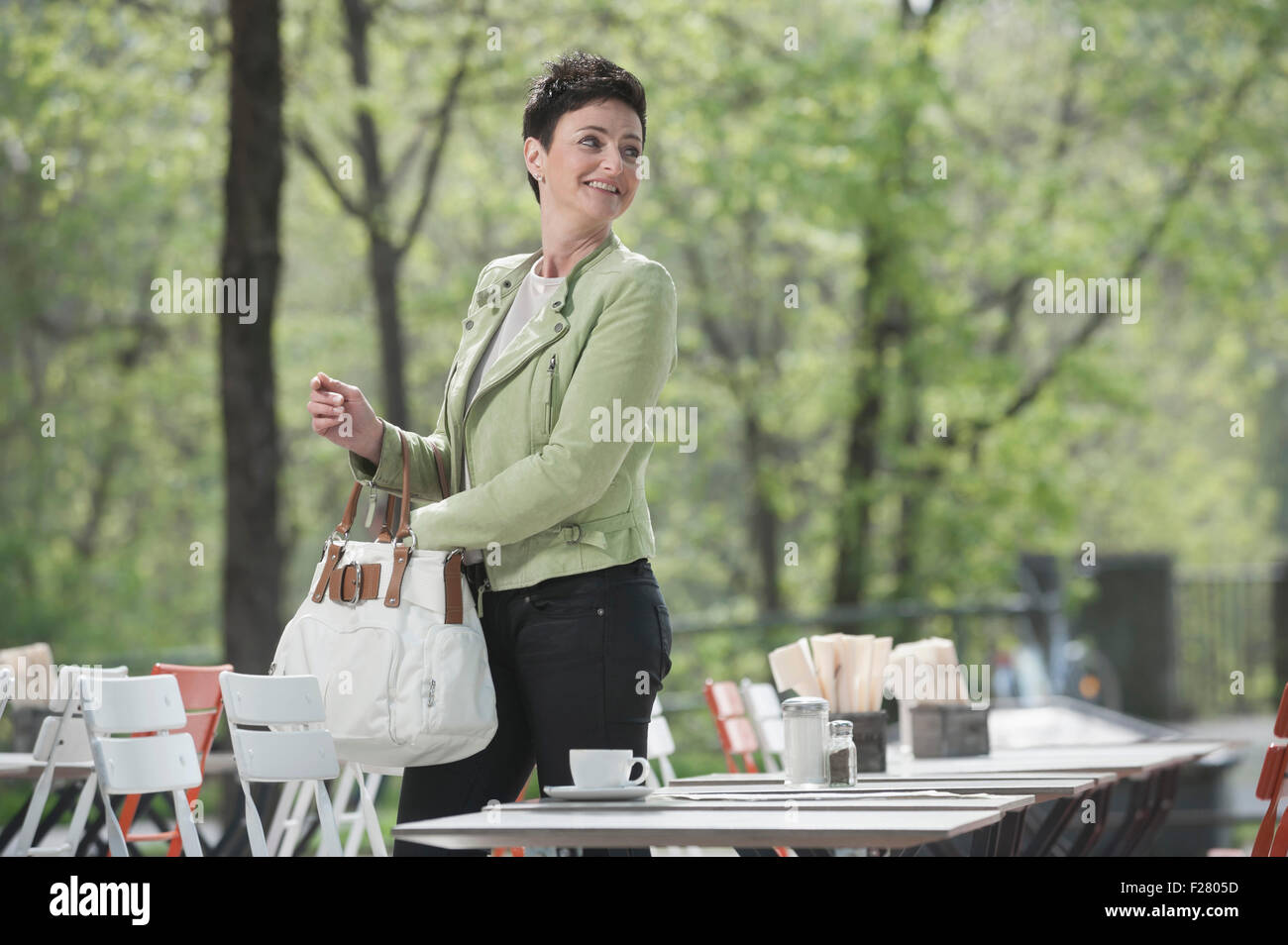 Mature woman with handbag looking over shoulder in the sidewalk cafe ...