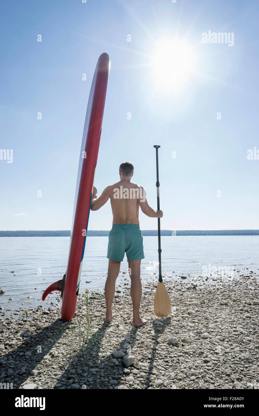 Mature man carrying paddleboard at lakeshore, Bavaria, Germany Stock ...