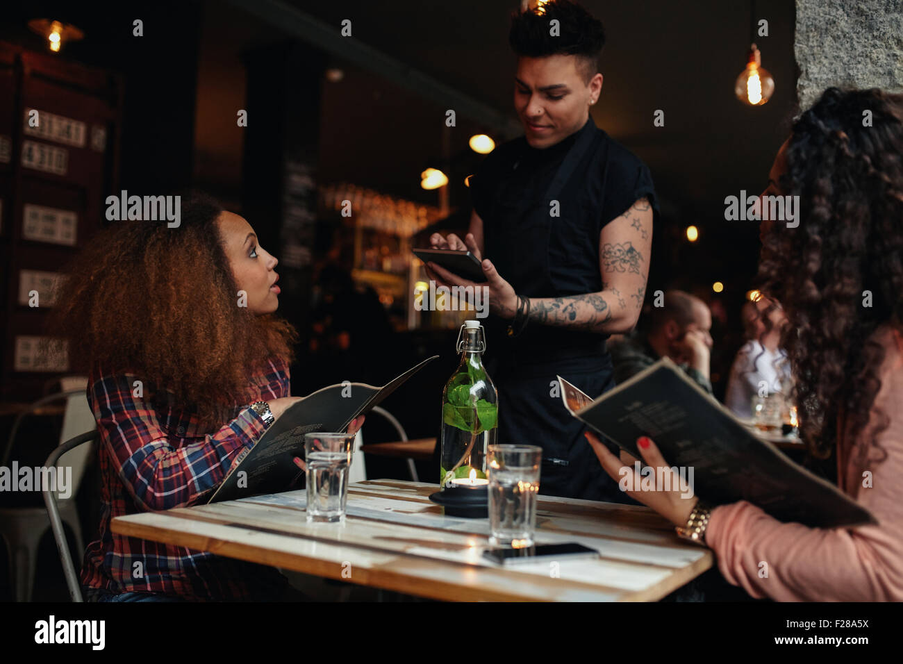Portrait of a young woman giving an order to a waiter at a cafe sitting ...