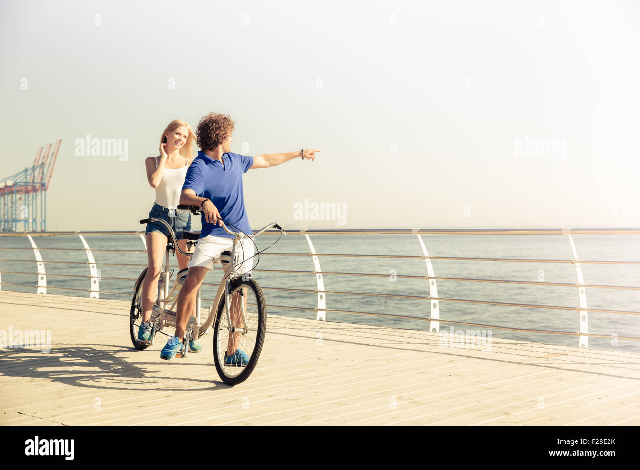 Portrait of a couple riding on tandem bicycle outdoors near the sea ...