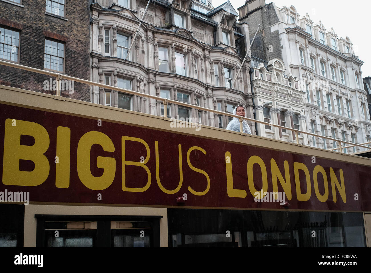 A man stands a lone figure on top of a open London bus in the rain ...