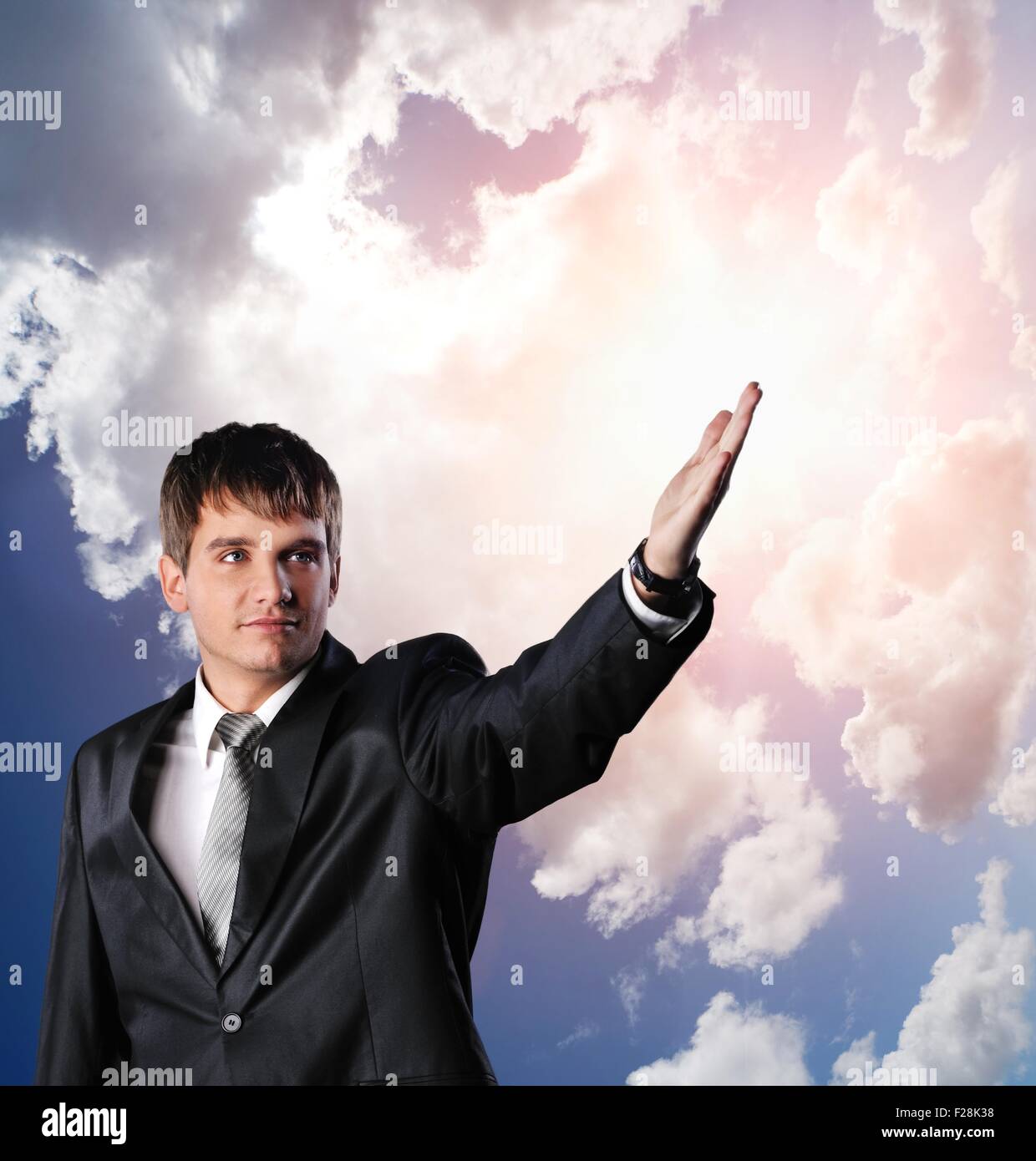 Handsome young businessman with outstretched hand against cloudy sky ...