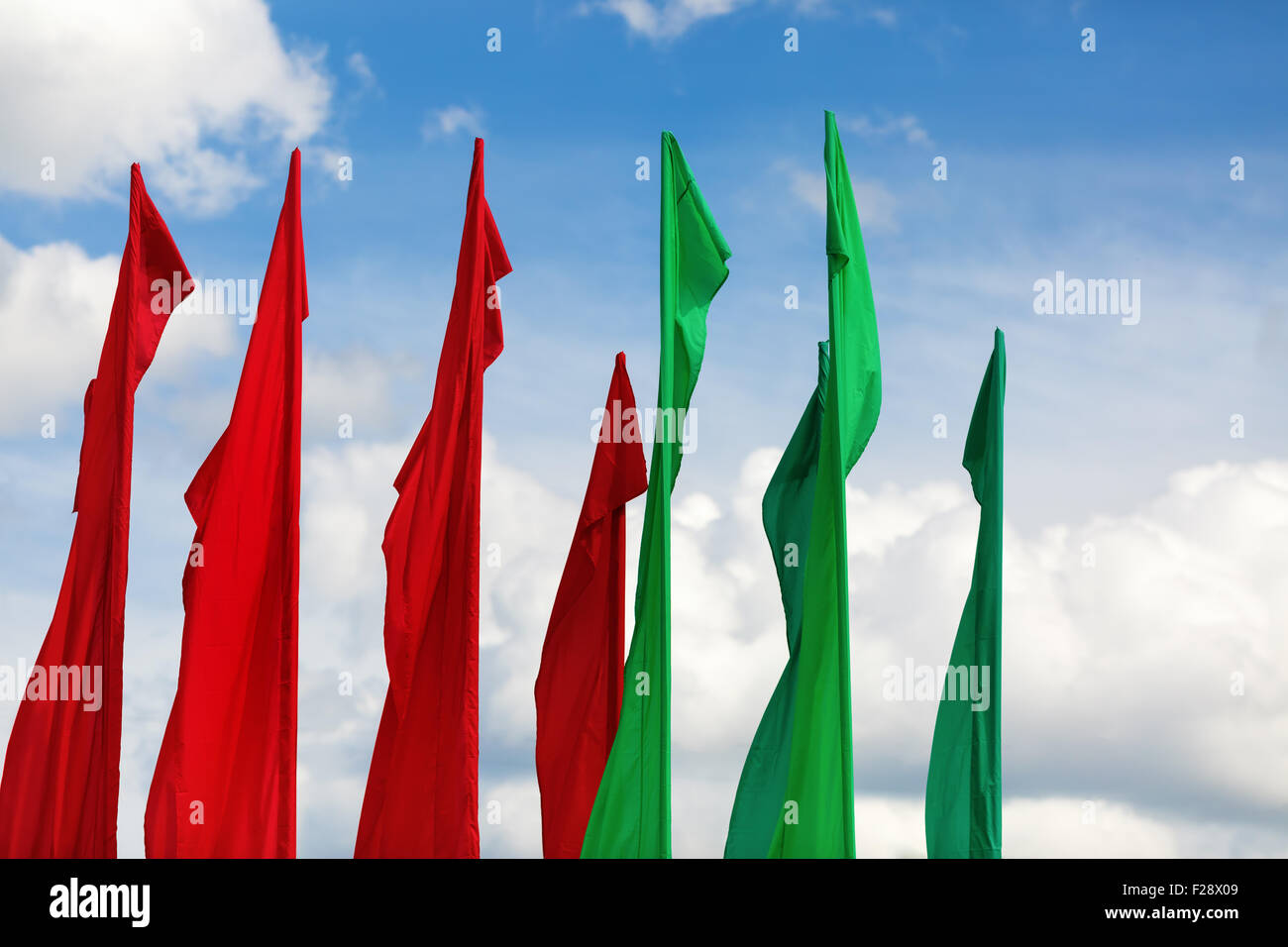 Several flagpoles with vertical green and red flag against a blue sky ...