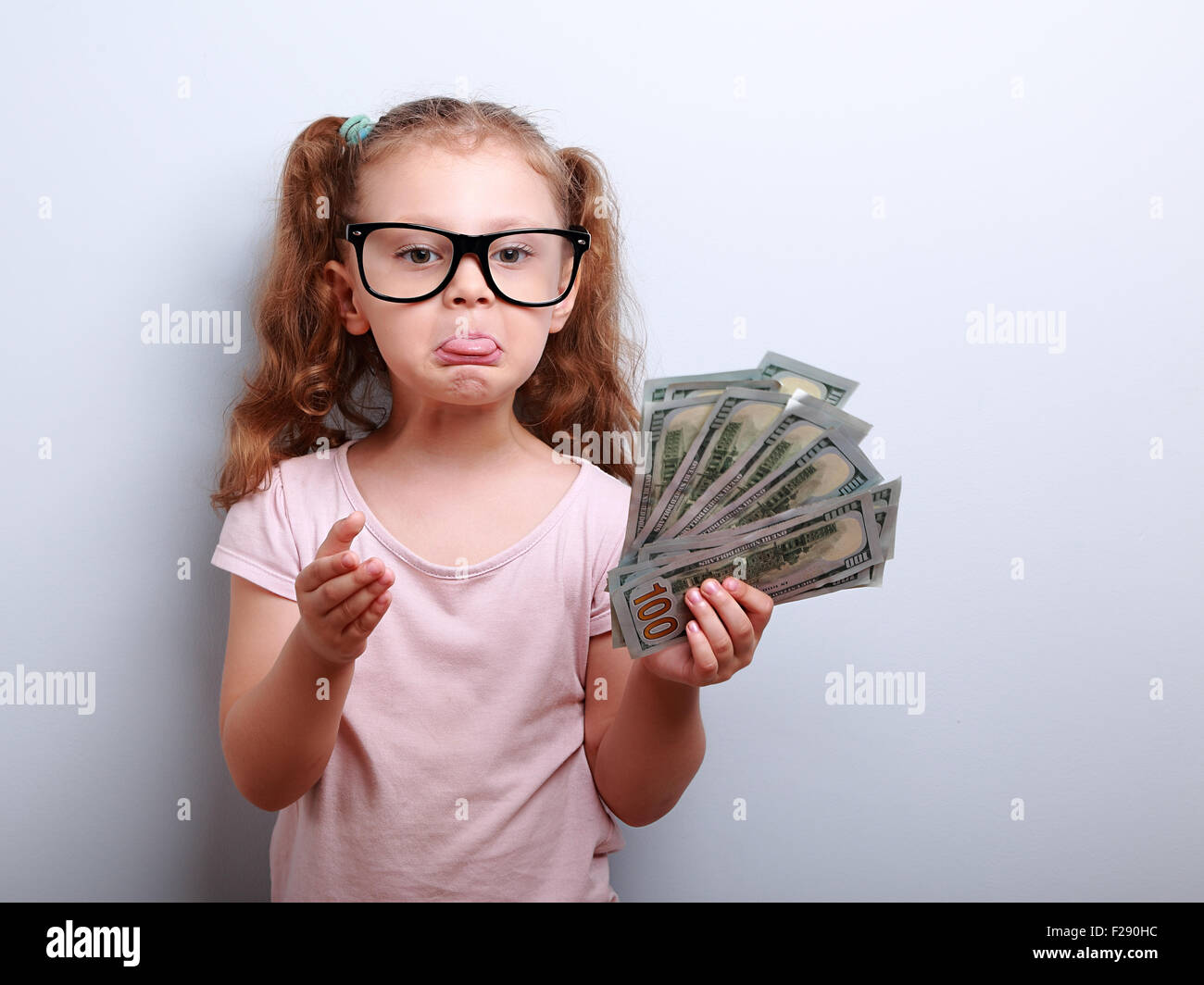 Fun grimacing kid girl explaining and showing tongue holding money in ...