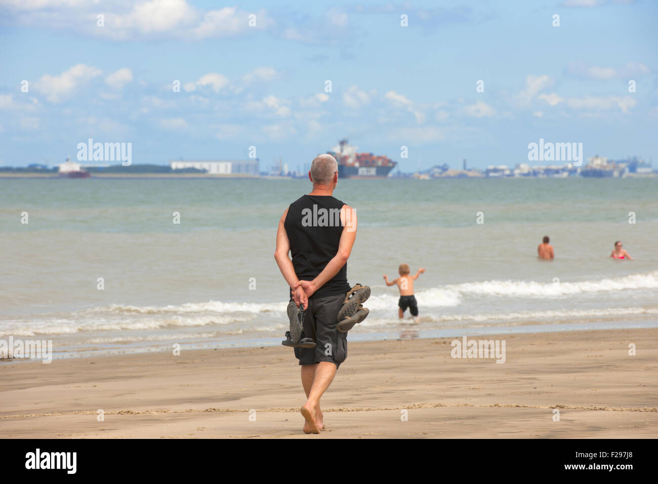 People walk on a sandy beach along the waterfront on a Summer day in ...