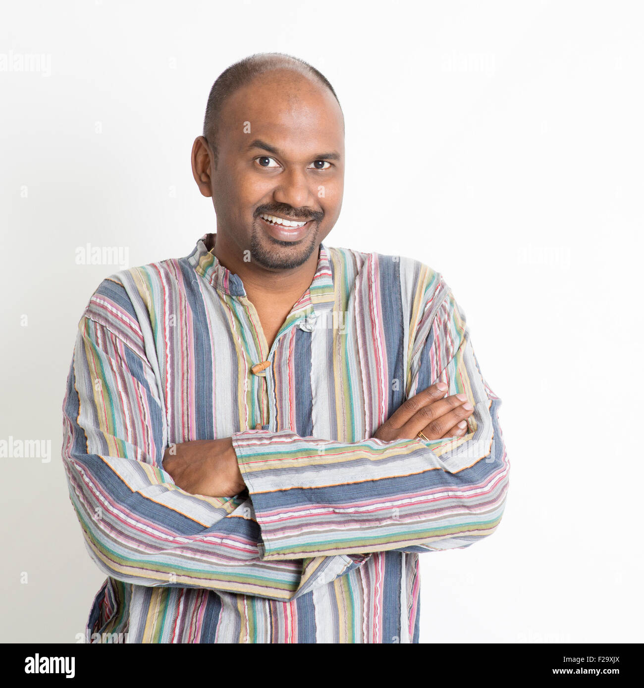 Portrait of smiling Indian man arms crossed on plain background with ...