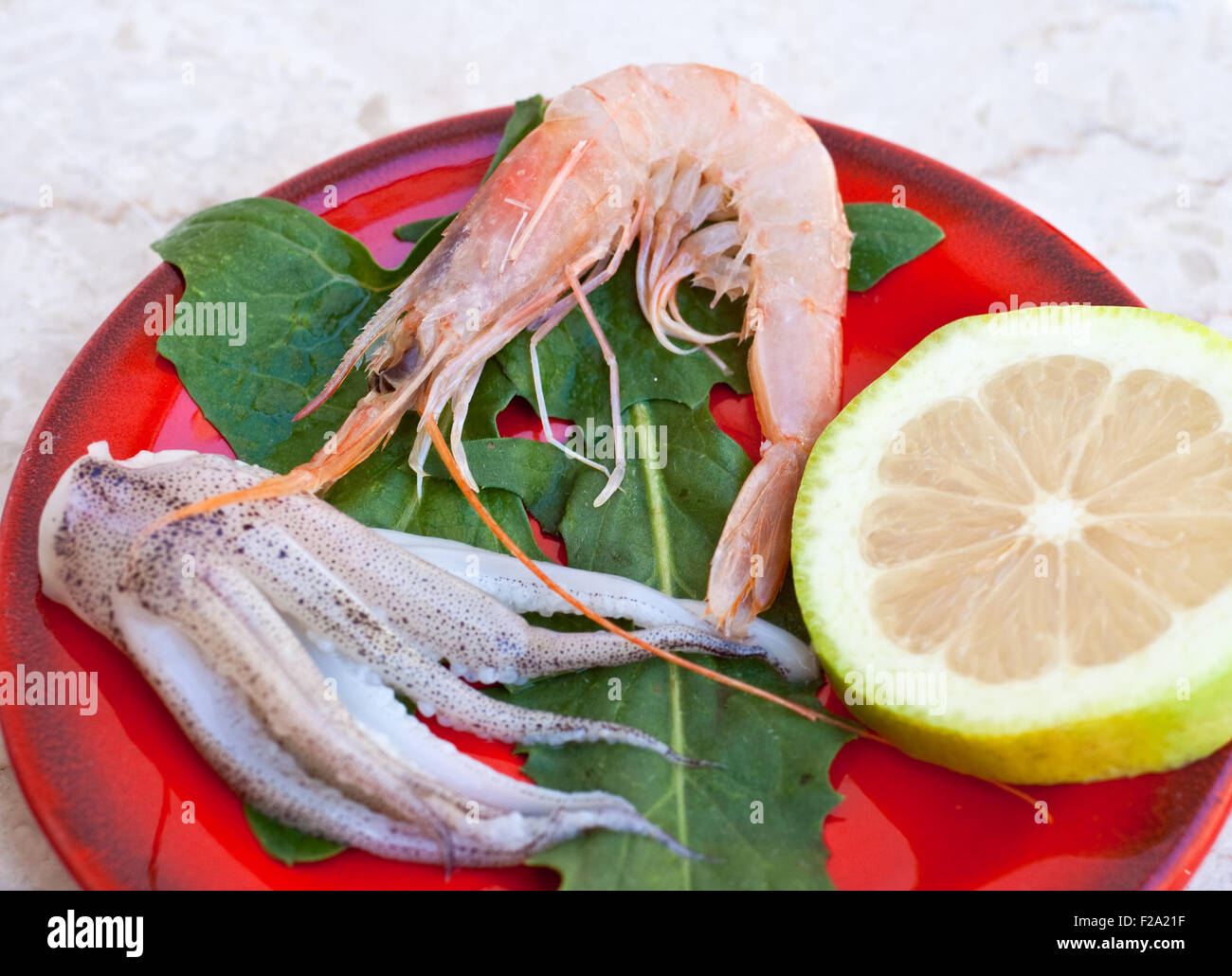Shrimp, cuttlefish and lemon inside a red saucer Stock Photo - Alamy