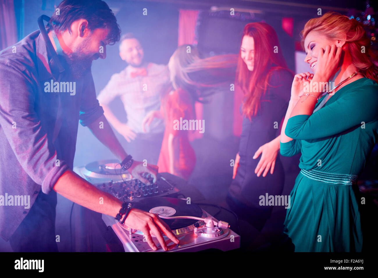 Glamorous girls dancing by dj adjusting sound on turntables in night ...