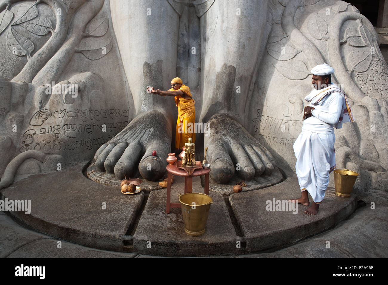 A jaïn pilgrim ( the man dressed in orange) is worshipping Gomateshwara ...