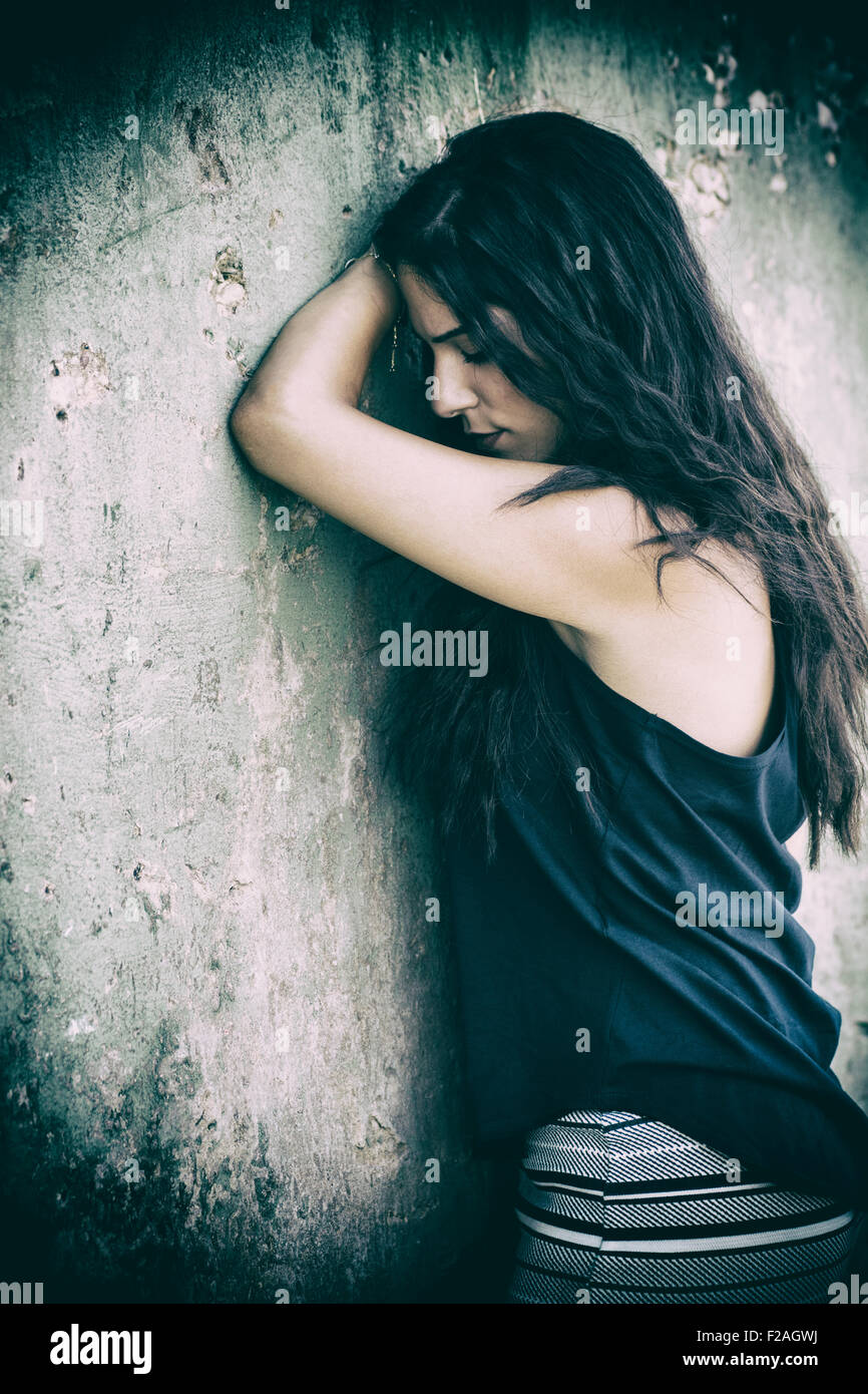 Miserable young woman leaning against the wall Stock Photo - Alamy