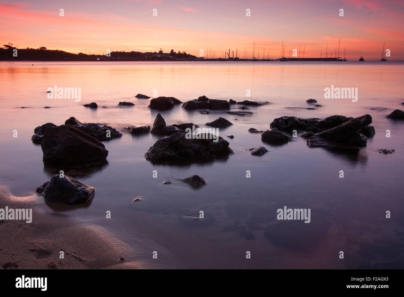 Sunset over boats with rocks in foreground Stock Photo - Alamy