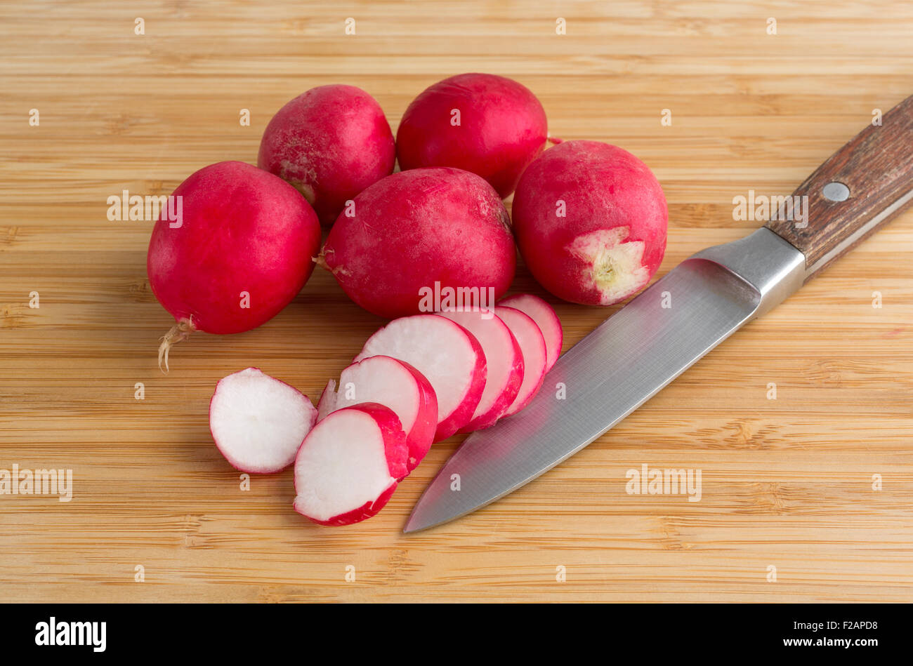 A sliced radish on a cutting board with a knife plus several whole ...