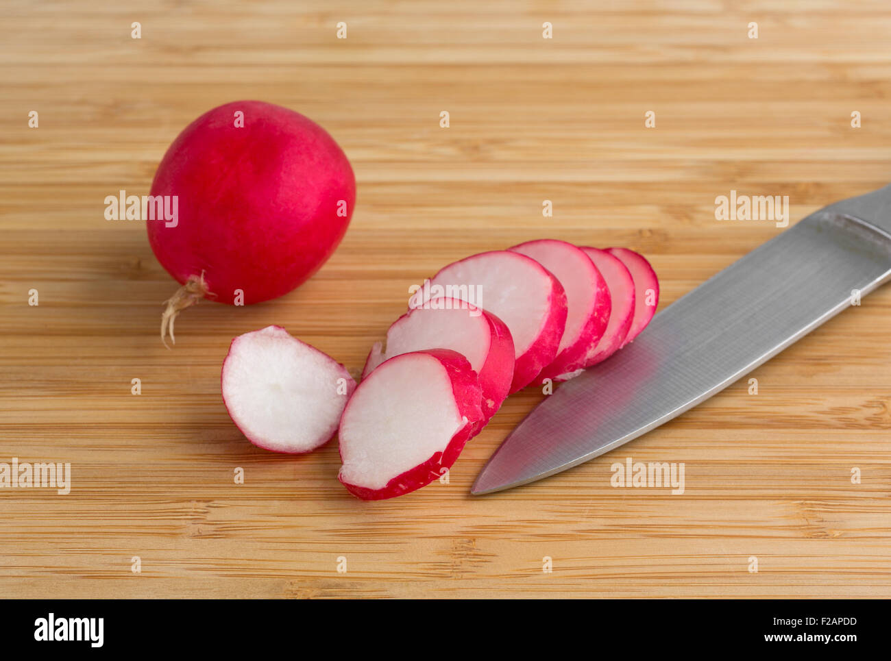 A sliced radish on a cutting board with a knife plus a single whole ...