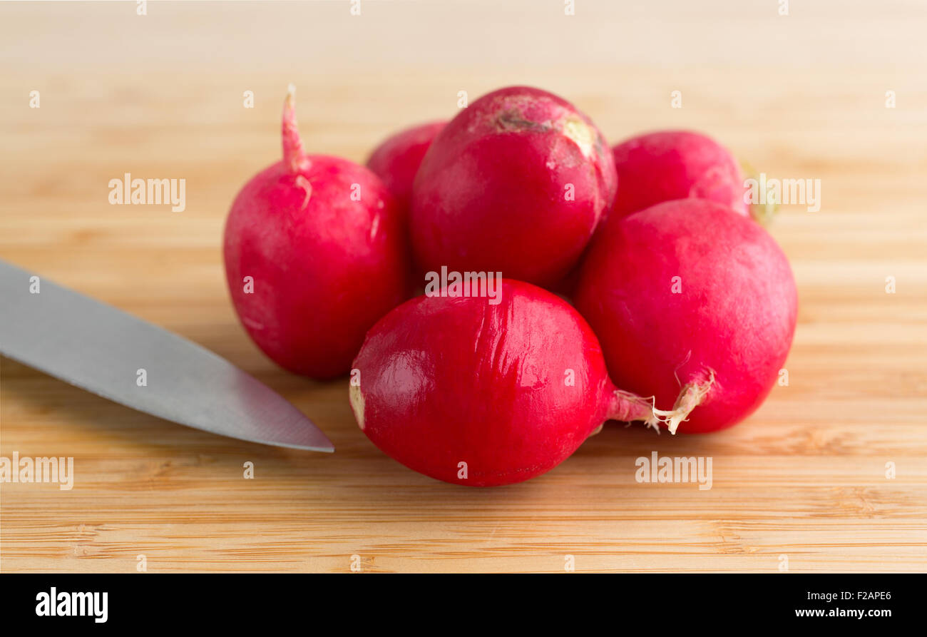 A group of radishes on a wood cutting board with a knife illuminated ...