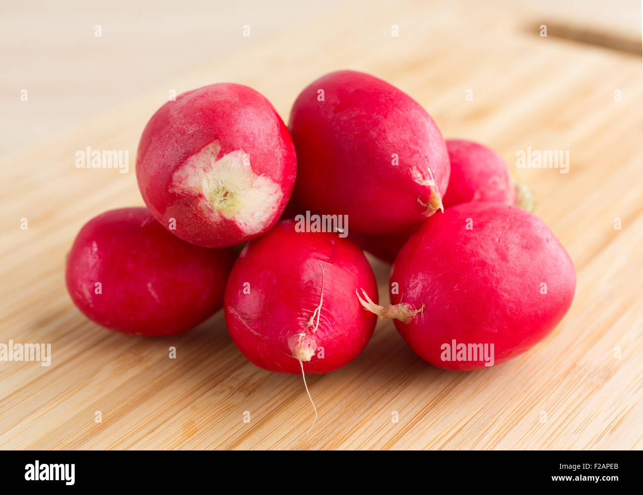 A group of fresh radishes on a wood cutting board illuminated with ...