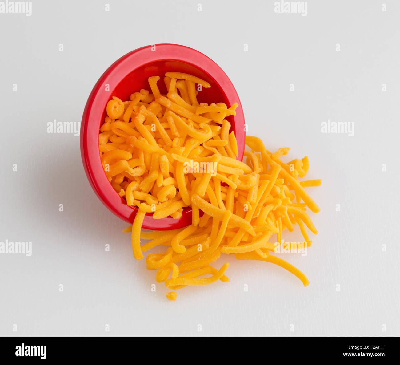 A small portion of shredded sharp cheddar cheese in a red bowl spilling ...