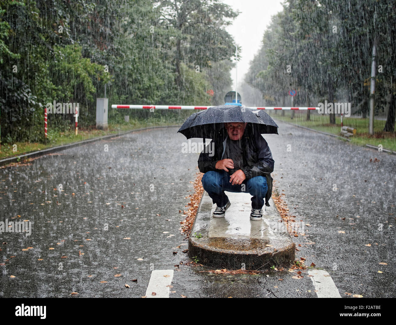 Male crouching under umbrella on a rainy day Stock Photo - Alamy