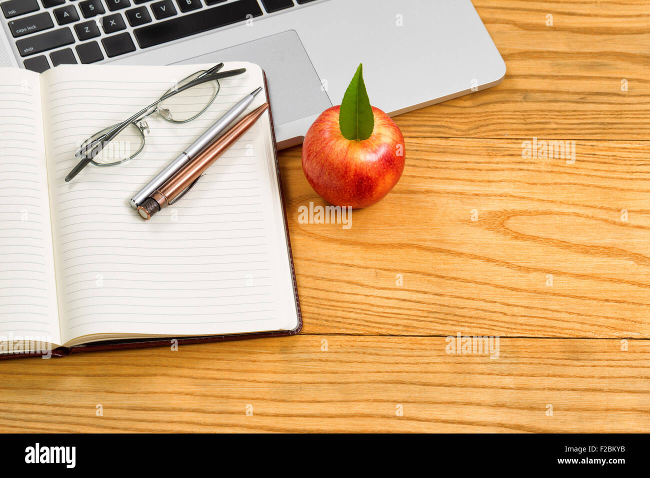 Top view of laptop computer with open notebook, reading glasses, apple ...