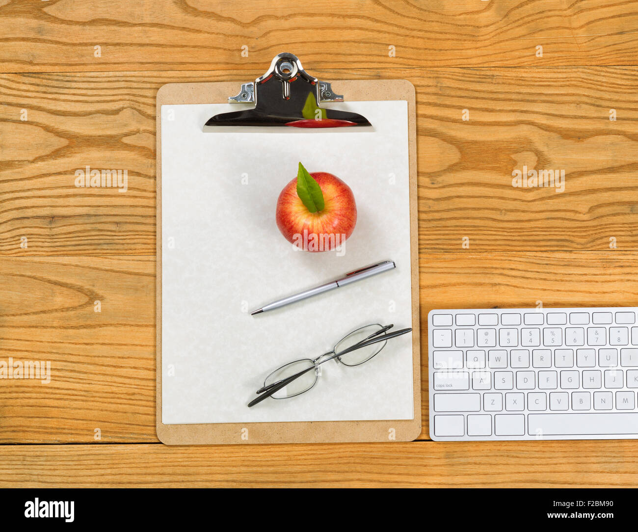 Top view of clipboard, computer keyboard, reading glasses, apple, paper ...