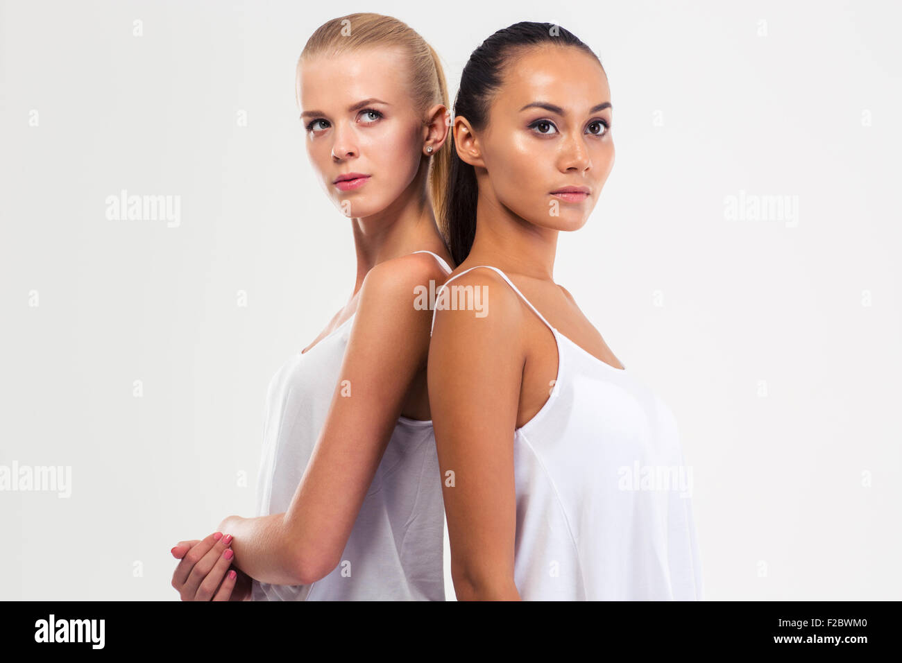 Portrait of a two beautiful girls standing back to back isolated on a ...