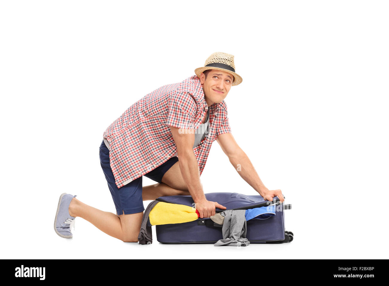 Frustrated guy trying to pack a lot of clothes into a single suitcase ...