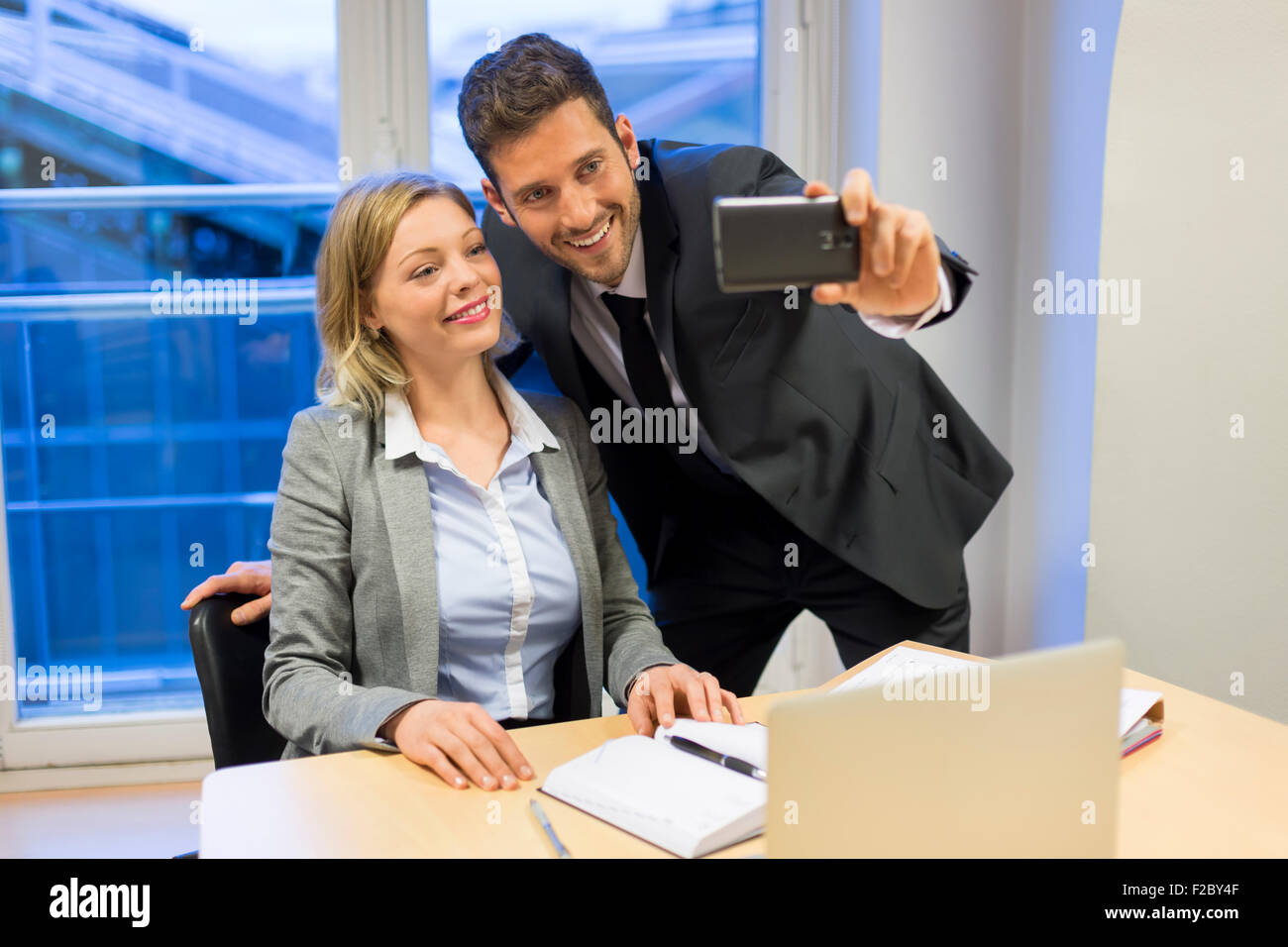 Portrait of two smiling business people taking a selfie with smartphone ...