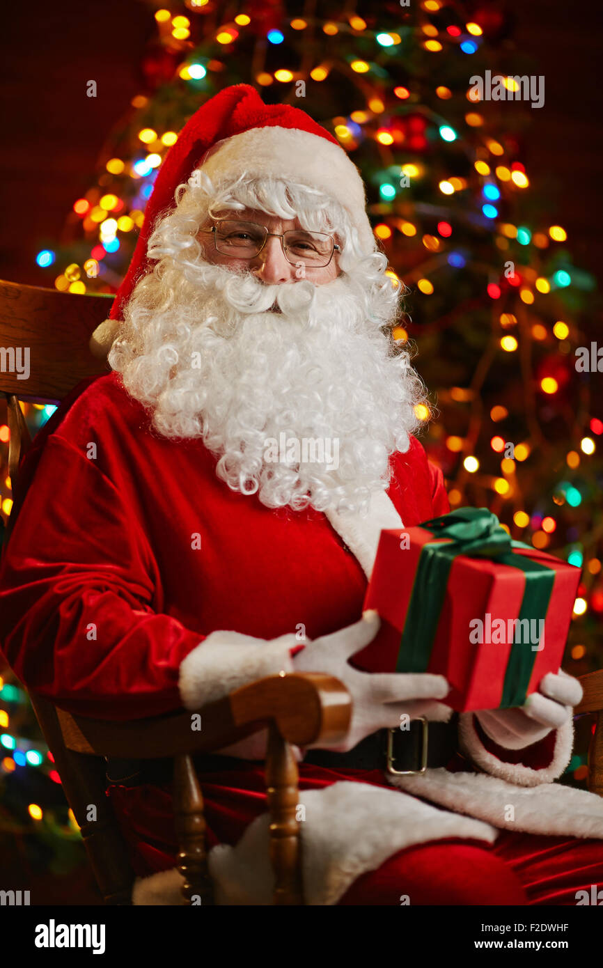 Happy Santa with box looking at camera while sitting by sparkling ...