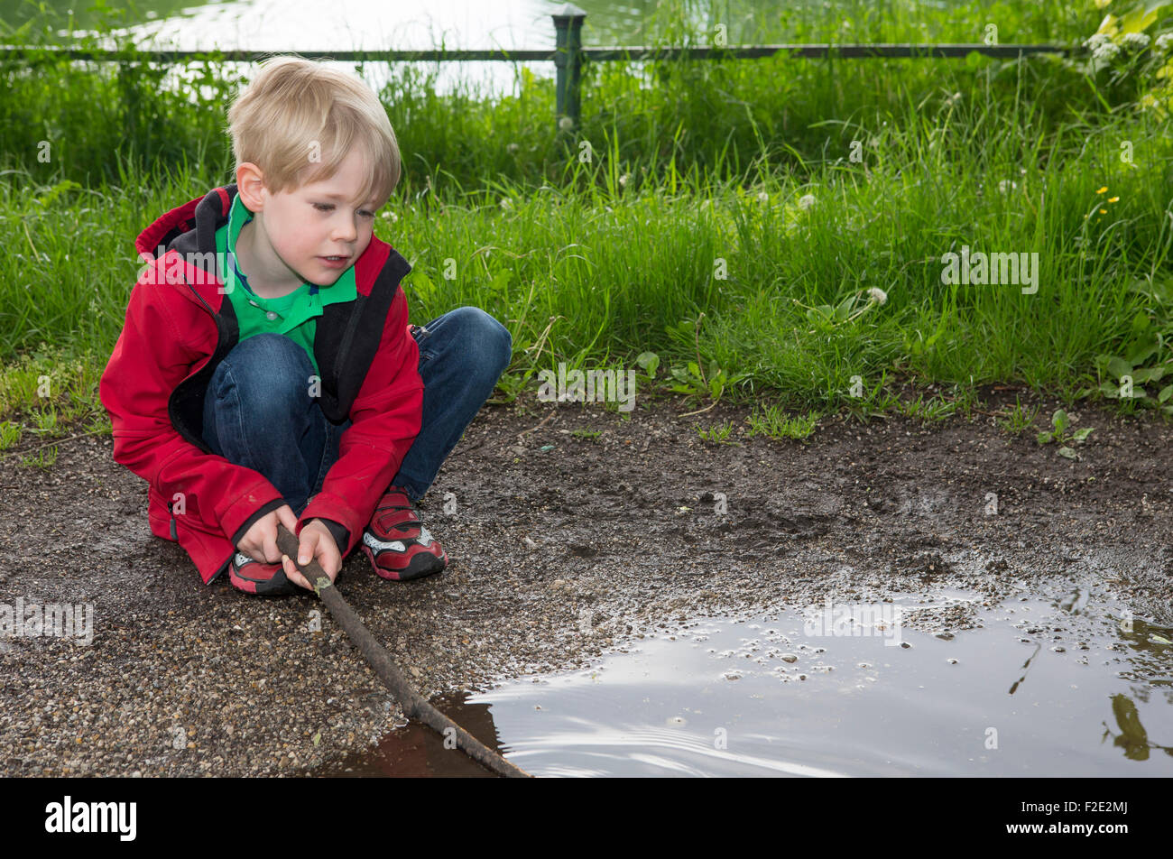 young blond boy playing with stick at a puddle Stock Photo - Alamy