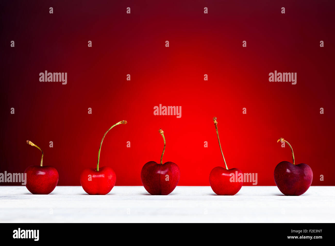 Row of freshly cherries on white wooden table over red background Stock ...
