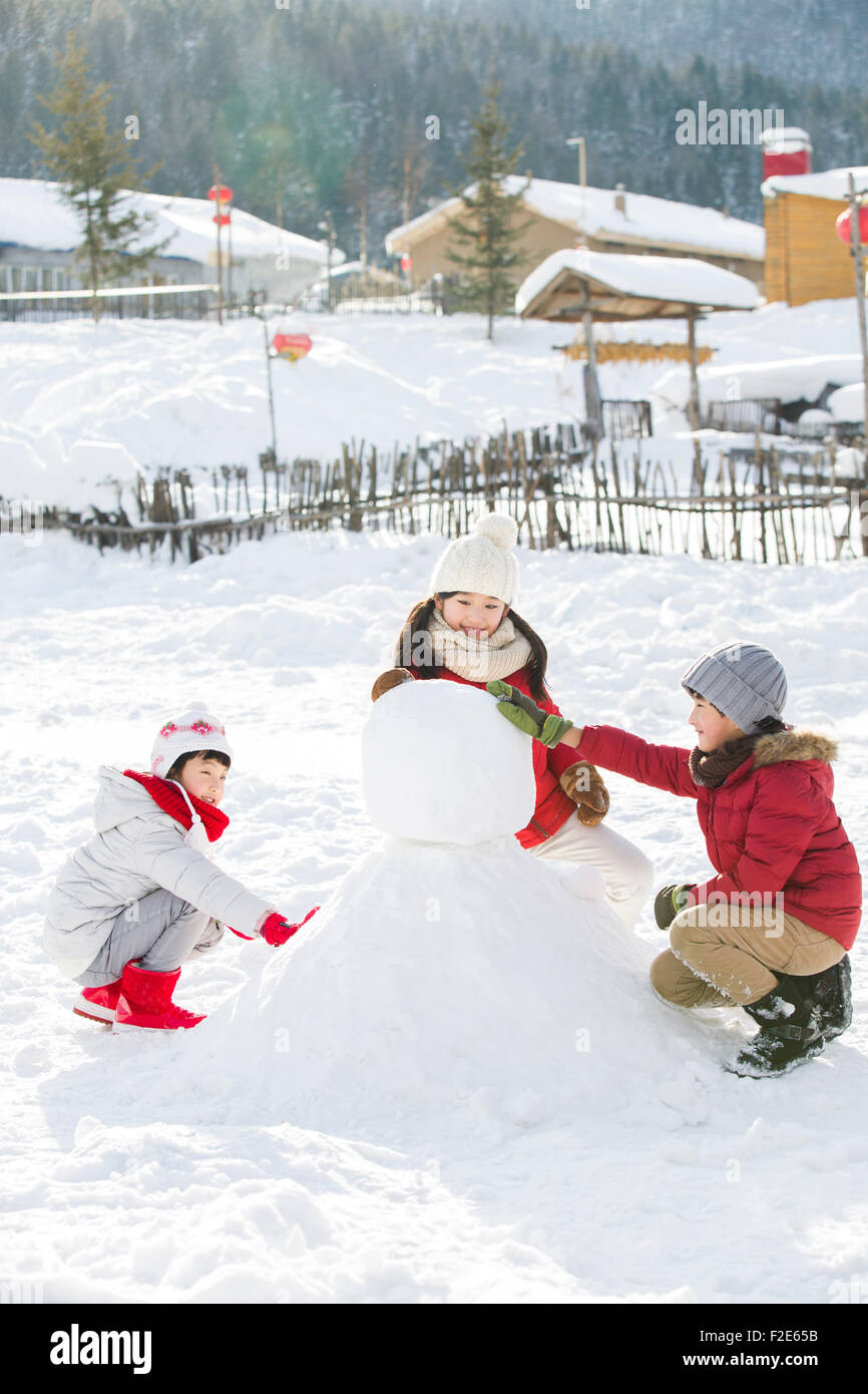 Happy children making snowman together Stock Photo - Alamy