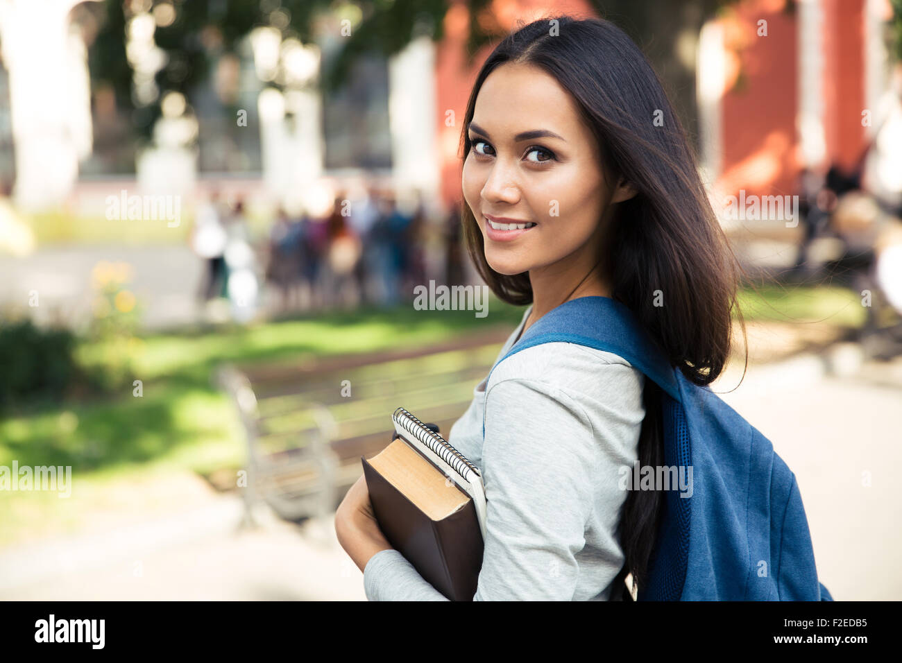 Portrait of a happy female student looking back at camera outdoors ...