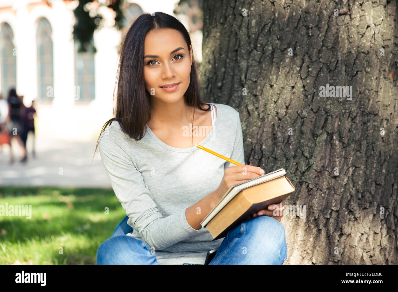 Portrait of a happy female student writing notes in notepad outdoors ...