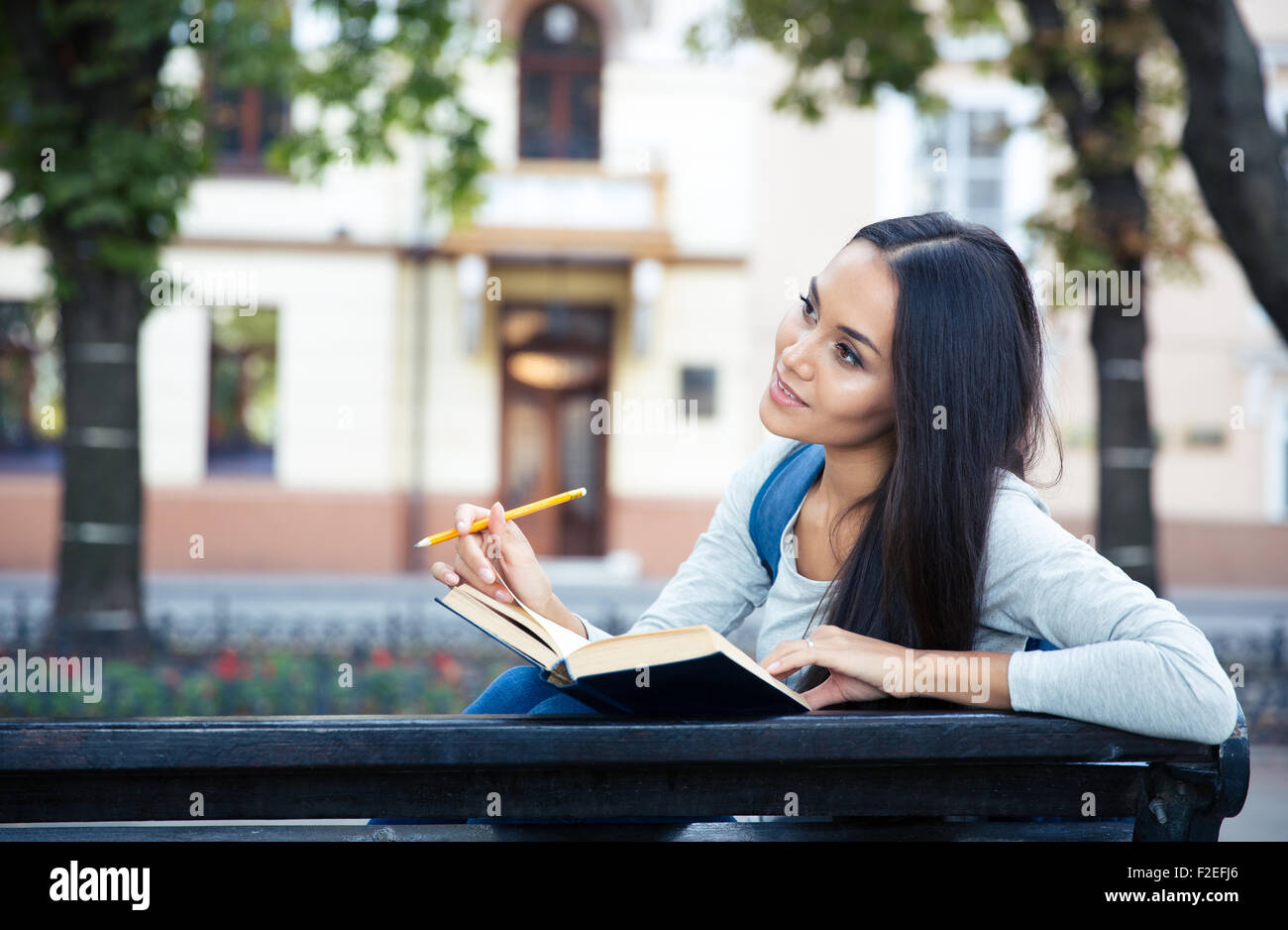 Portrait of a thoughtful female student sitting on the bench with book ...