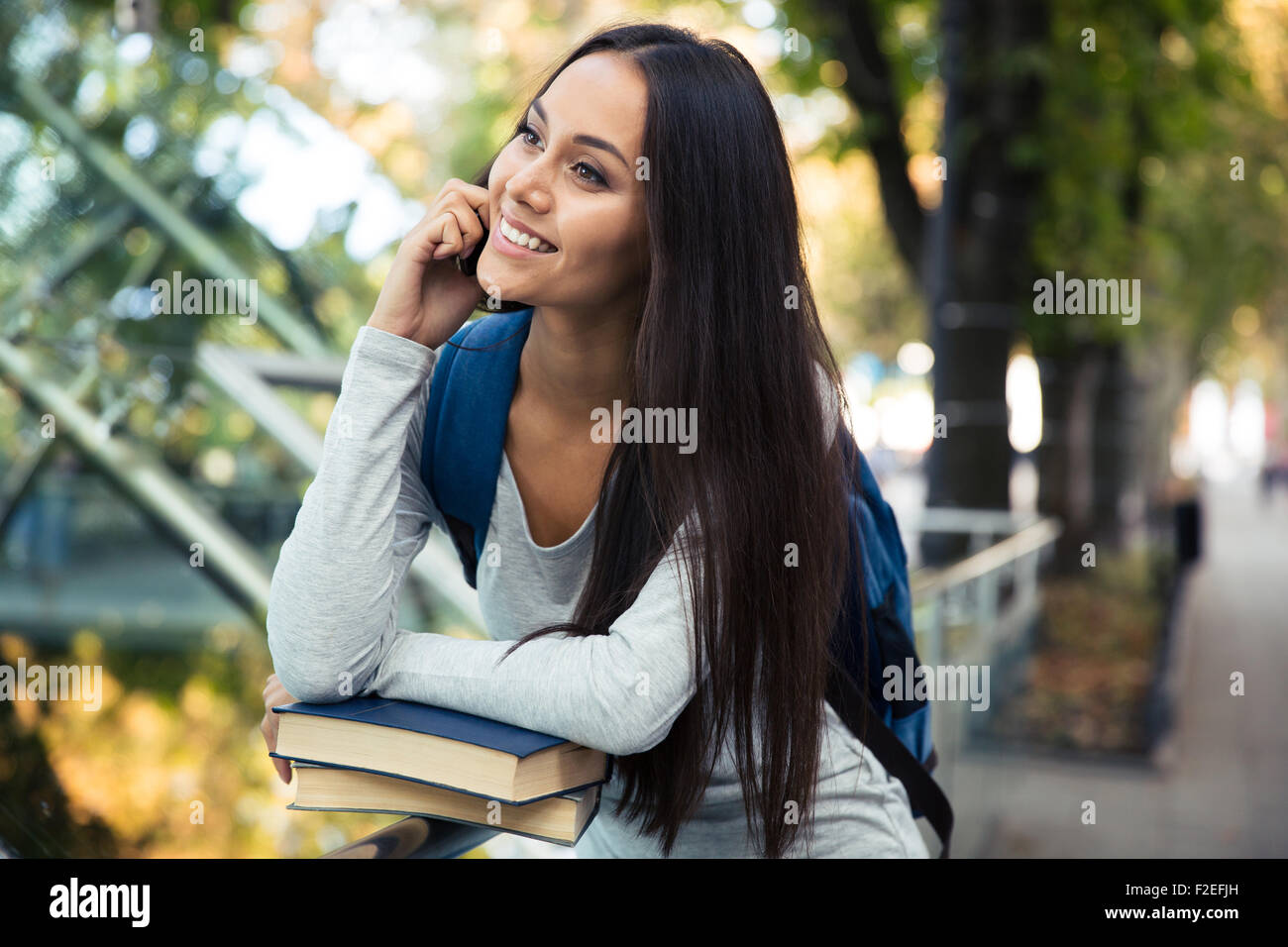 Portrait of a smiling female student talking on the phone outdoors ...