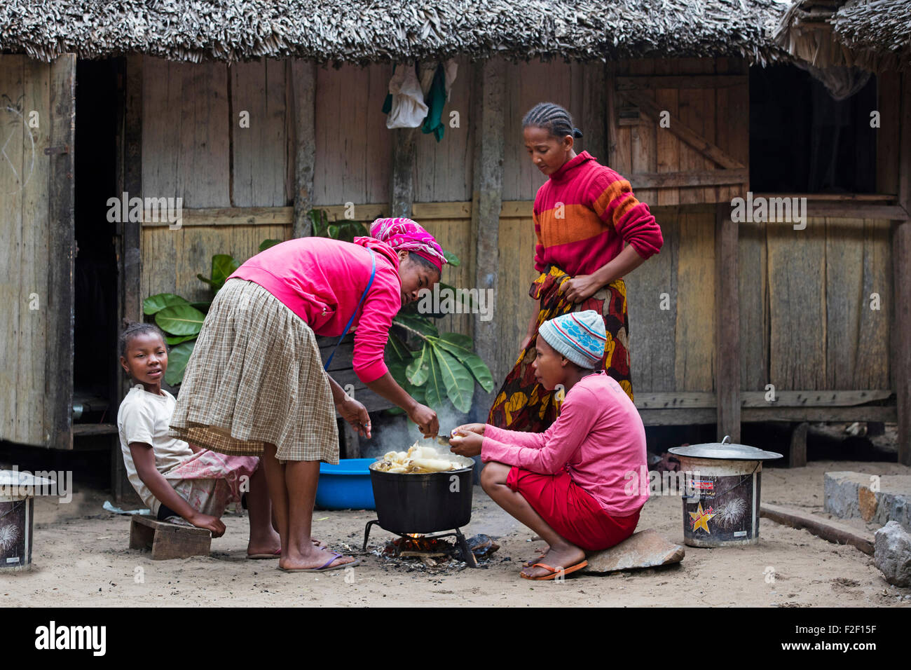 Malagasy family cooking maniok in front of traditional wooden house in ...