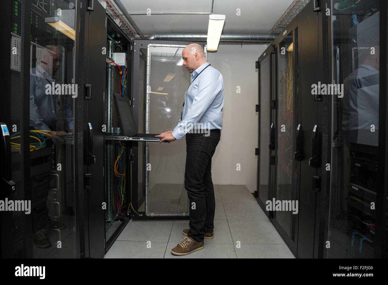 Computer specialist working on servers in a server room, looking at ...