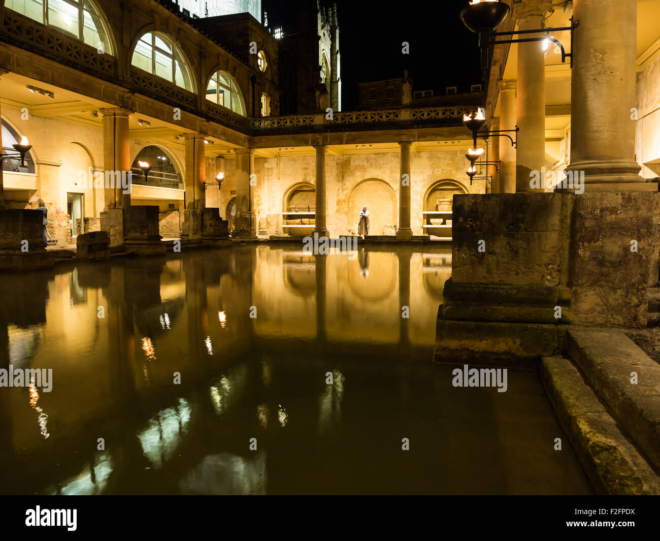 A roman stands at the edge of the famous Roman bath at night lit by ...