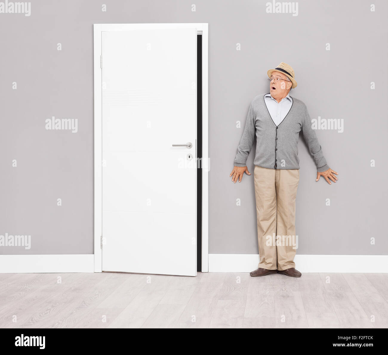 Scared senior gentleman hiding by leaning against a wall next to an ...