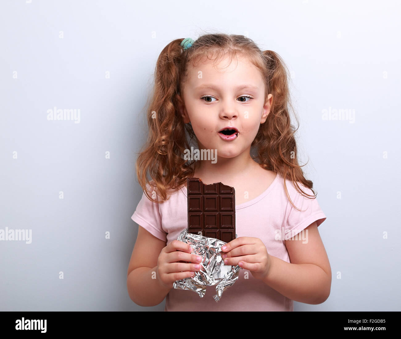 Fun kid girl eating dark chocolate and amazing how it tasty on blue ...