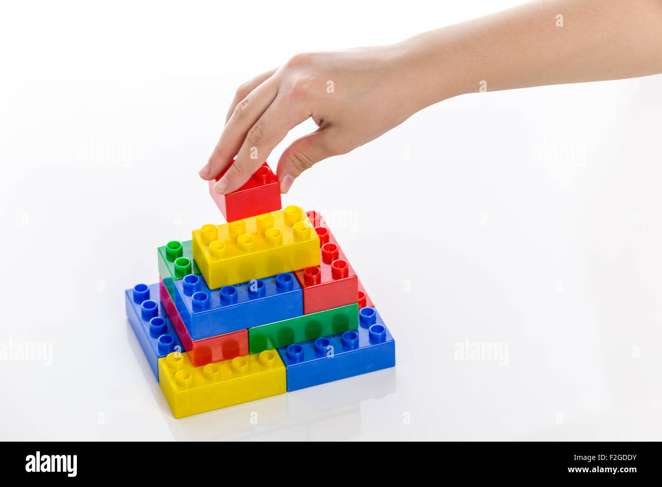 Hand completing colorful plastic brick structure on white background ...