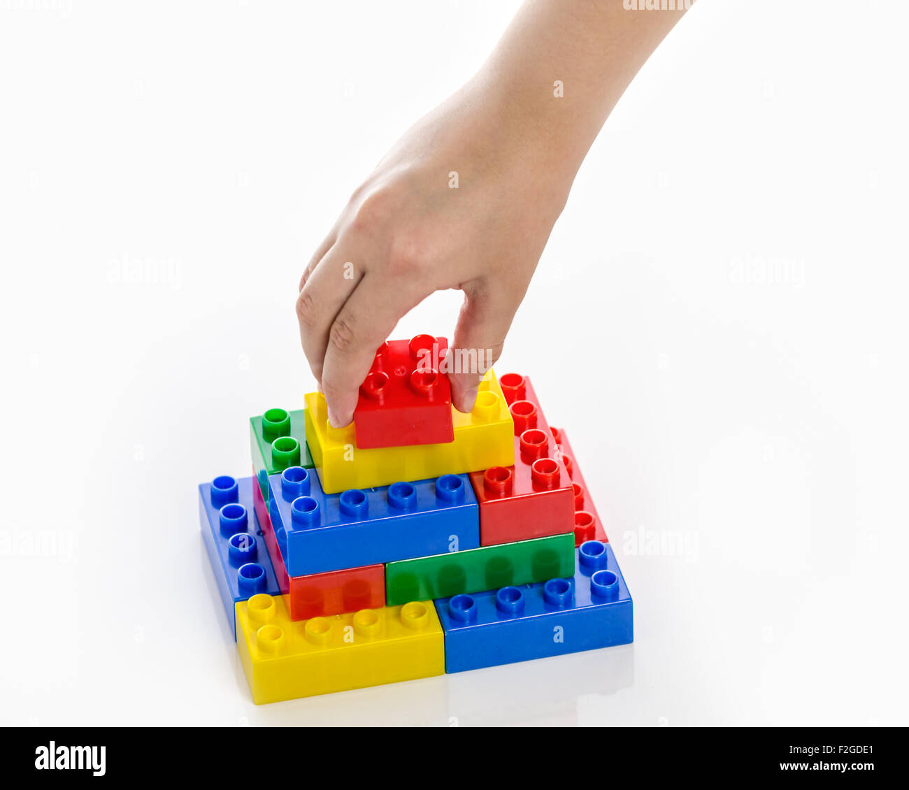 Hand completing colorful plastic brick structure on white background ...