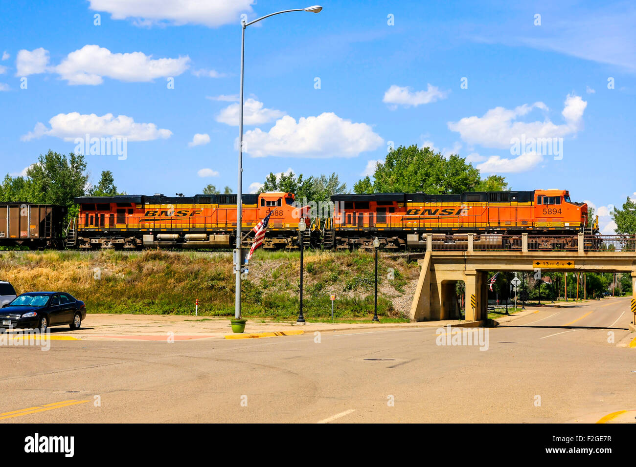 An orange BNSF locomotive passes over a bridge on the main line between ...