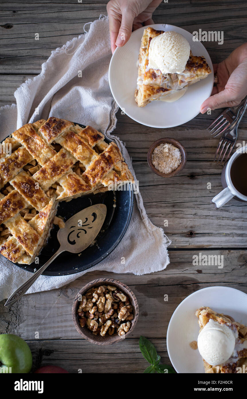 A slice of apple pie is being served by a woman on a farm style table ...