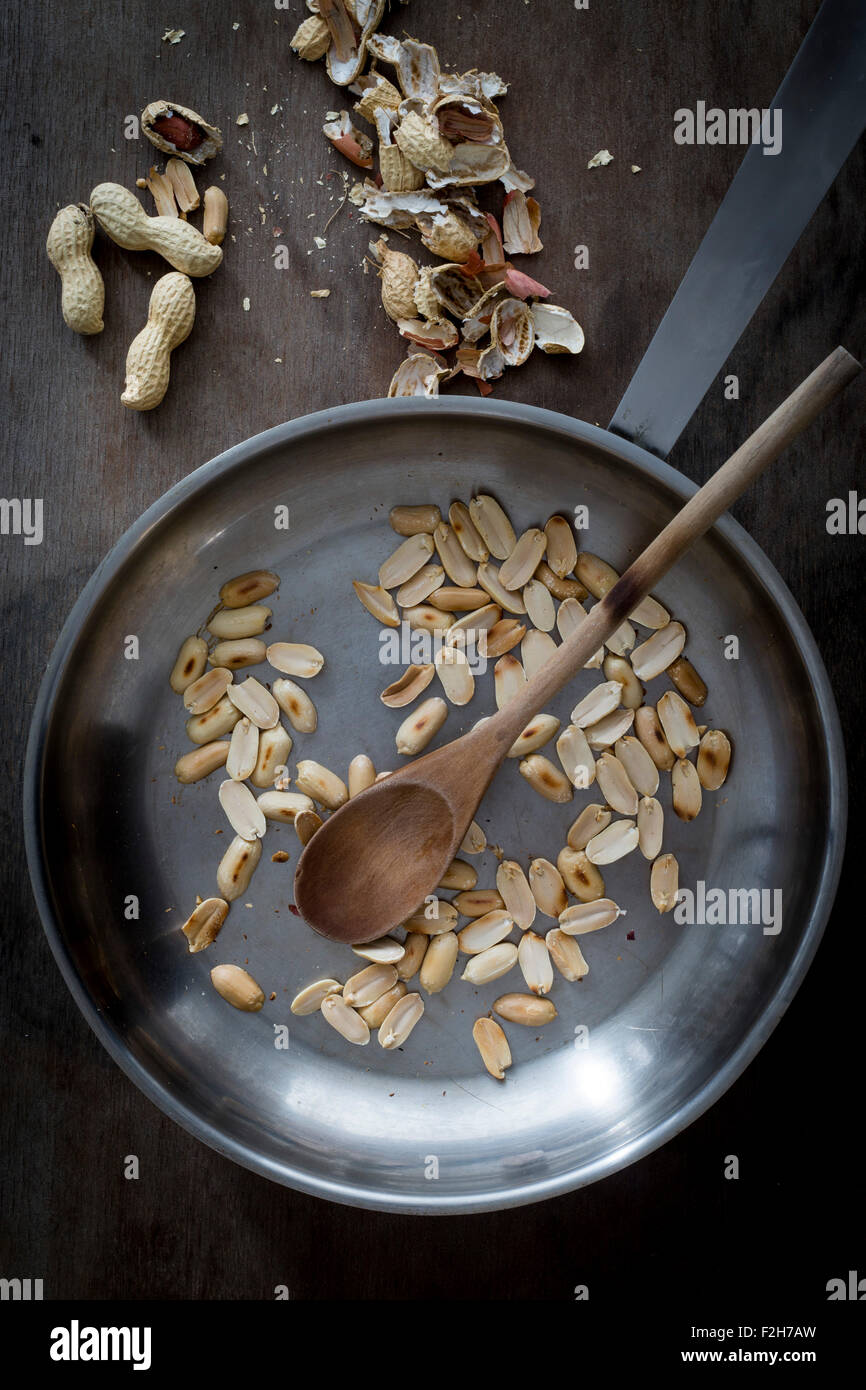 Roasted peanuts in steel skillet with wooden spatula on wooden tabletop ...
