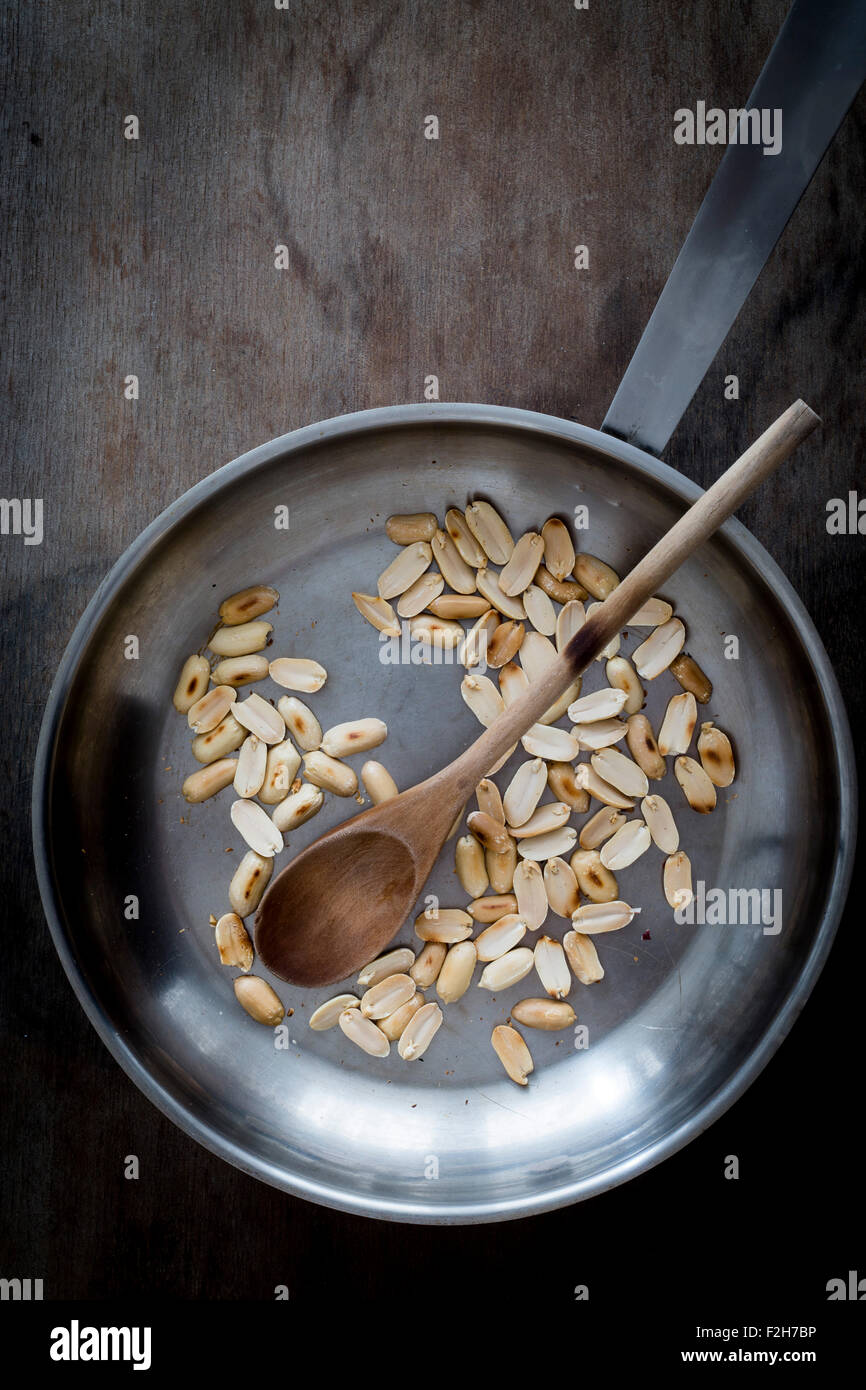Roasted peanuts in steel skillet with wooden spatula on wooden tabletop ...