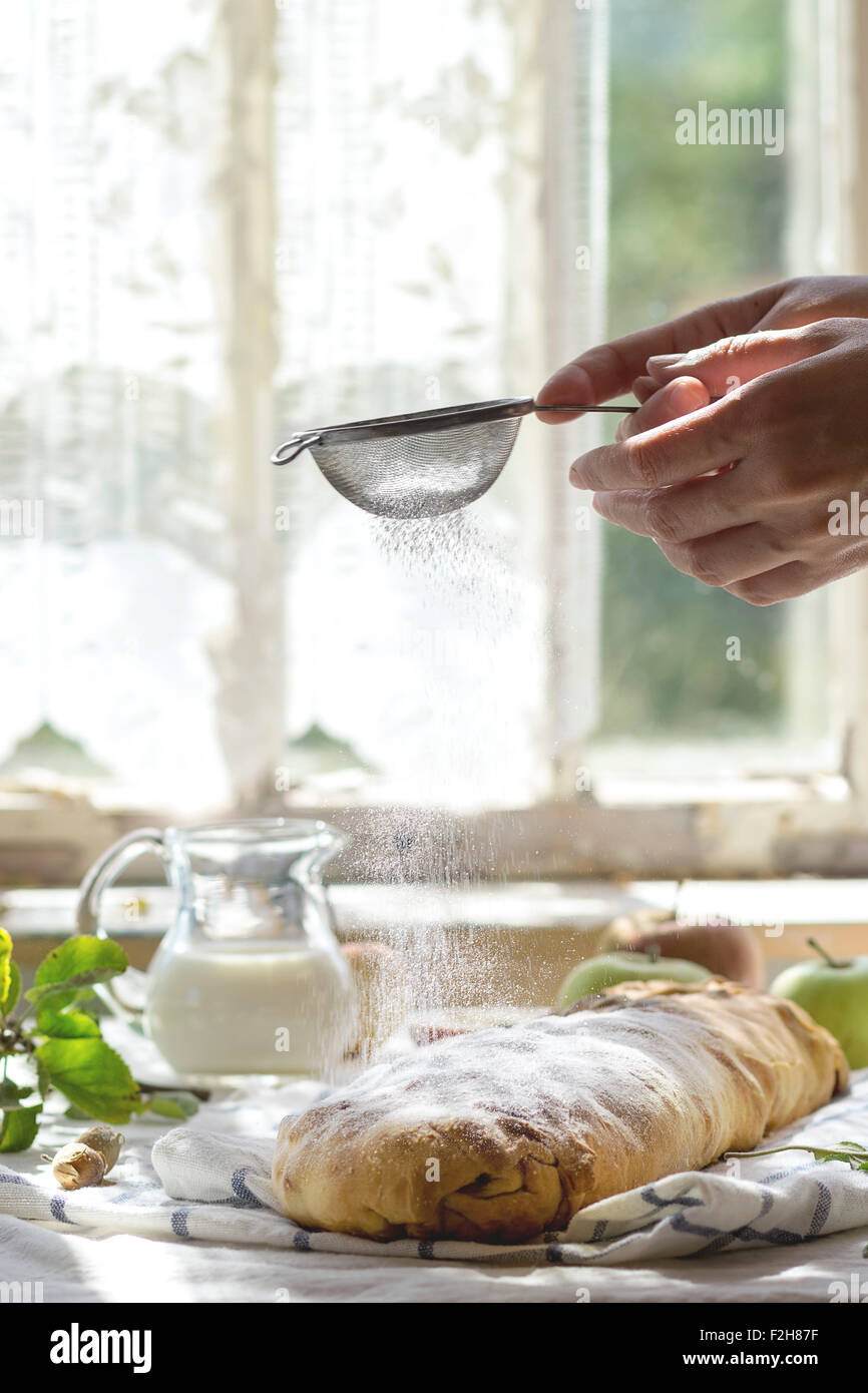 Woman's hand sprinkle with powdered sugar fresh baked homemade apple ...