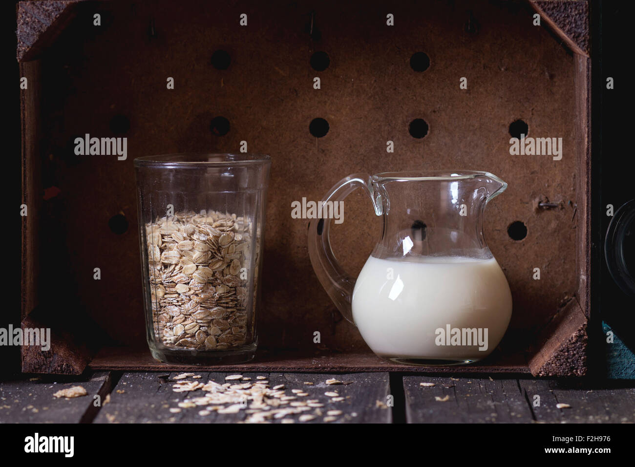 Glass jug of non-dairy oat milk and retro glass of oat flakes in wooden ...